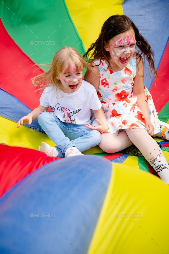 Two excited laughing girls having fun in multicoloured play parachute ...