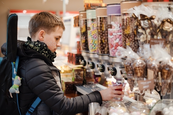 Preteen boy filling a jar with candies in the confectionery. Boy buying ...