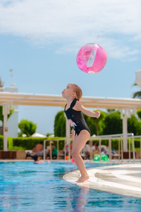 Cute little girl in black swimsuit playing with pink inflatable ball ...
