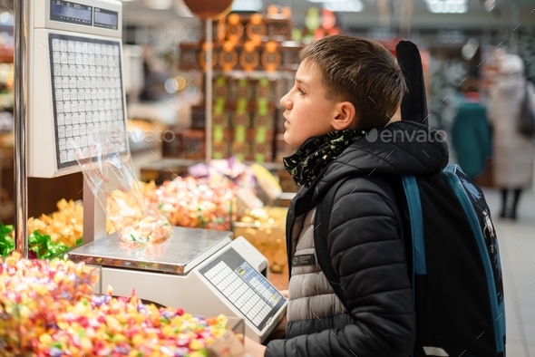 Boy with a backpack weighing sweets on the scale in the self service ...