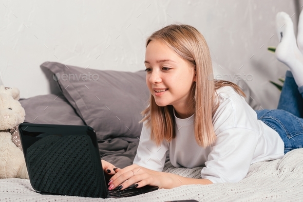 Video communication.Teenage girl lying on the bed and communicating via ...