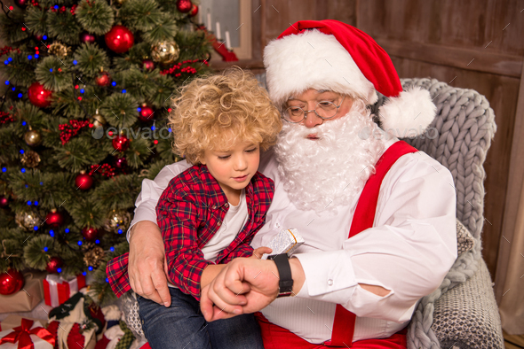Santa Claus sitting on armchair with kid on knee and and looking at ...
