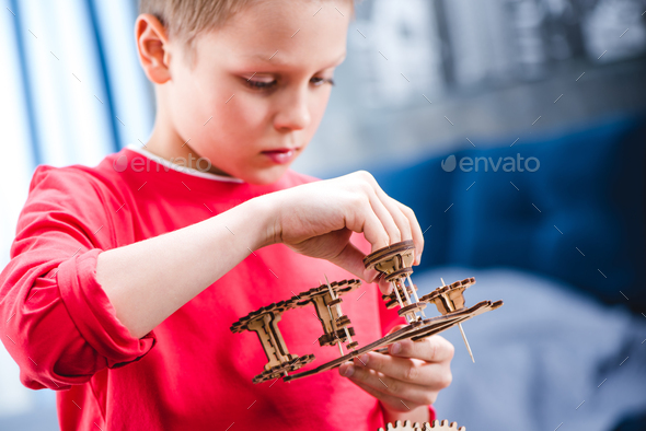 Close-up portrait of concentrated kid holding wooden gear mechanical ...