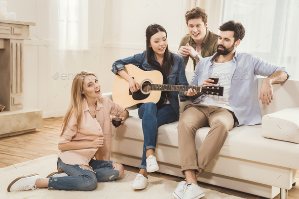 Diverse people partying together at dining room, playing acoustic ...