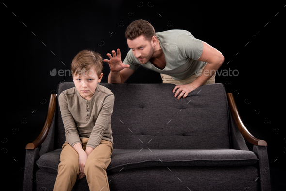 Angry father gesturing to scared little son sitting on sofa, family ...