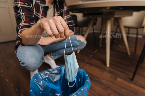 cropped view of young man throwing medical mask in trash can with ...