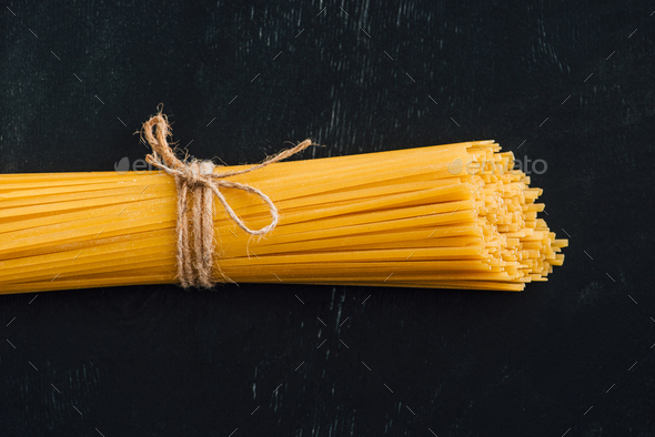 top view of raw Italian spaghetti tied with string on black background ...