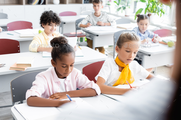 selective focus of multicultural pupils writing in notebooks during ...