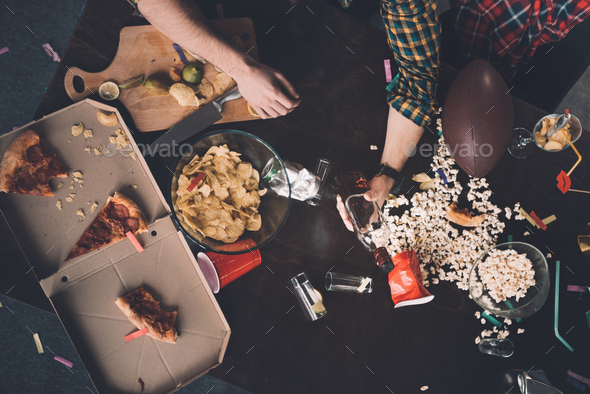Partial top view of man holding whiskey bottle at messy table after ...