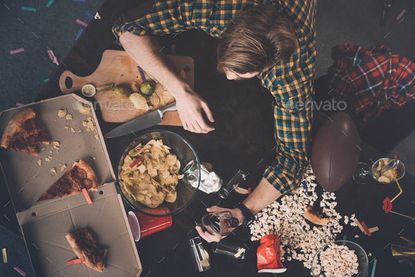Overhead view of young man with whiskey bottle at messy table after ...