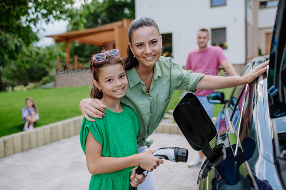 Happy mother showing her little daughter how to charge their electric ...