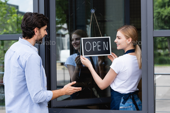 Customer pointing with hand near smiling waitress holding signboard ...