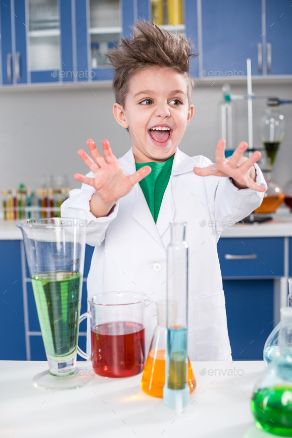 Excited little boy in lab coat making experiment in chemical laboratory ...