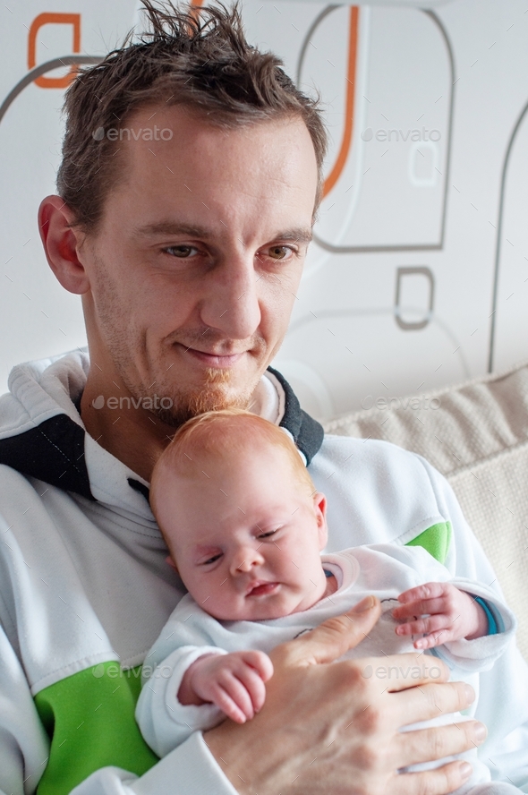 little tired dad smiles and rocks the little red-haired baby to sleep ...