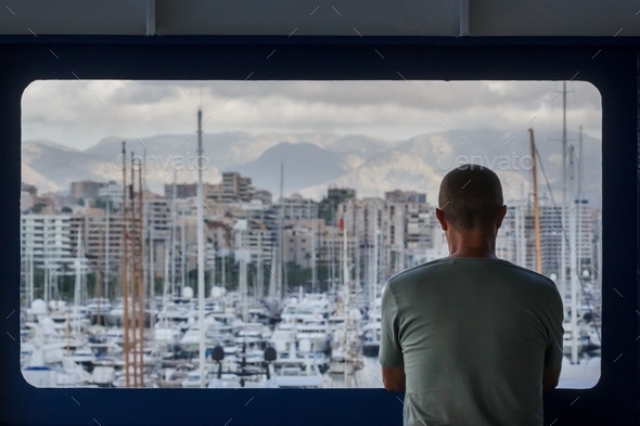Man looking through a window in a ferryboat with the port at the ...