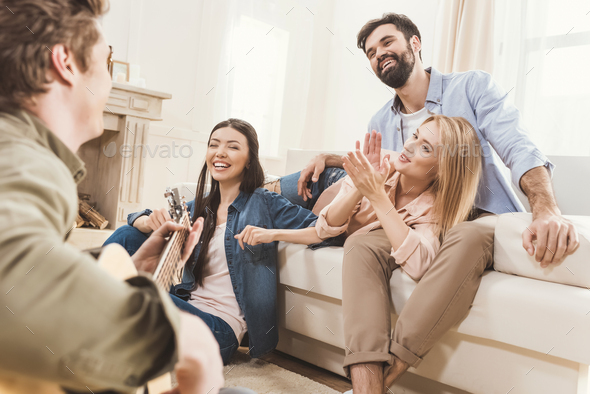 Diverse people partying together at dining room, playing acoustic ...