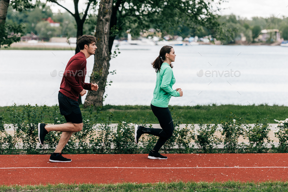 Side view of couple running on running track in park Stock Photo by ...