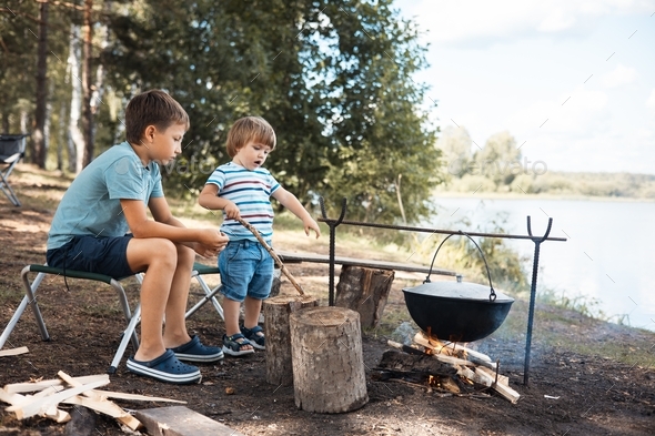 Children sitting around a campfire in forest in summer. Picnic outdoors ...