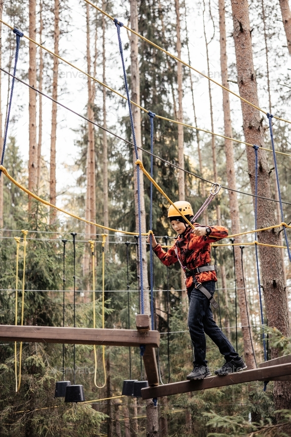 Teenager boy in safety equipment outing and climbing in adventure rope ...