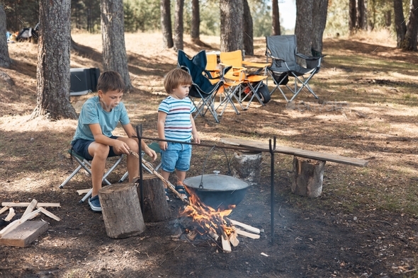 Children sitting around a campfire in forest in summer. Picnic outdoors ...