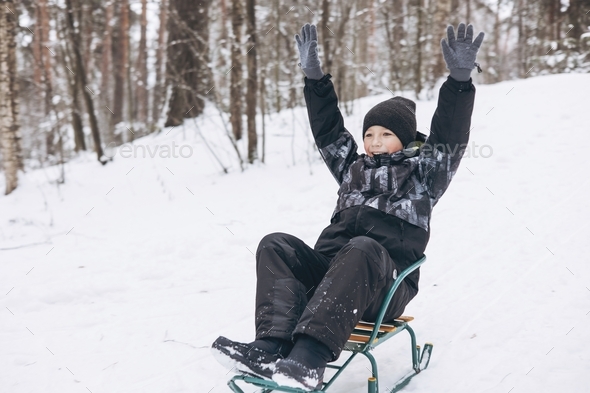 Happy teenager boy sledding and having fun in winter snowy forest ...