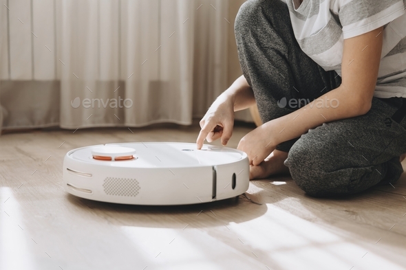 Teenager boy hand push start button on robotic vacuum cleaner for ...