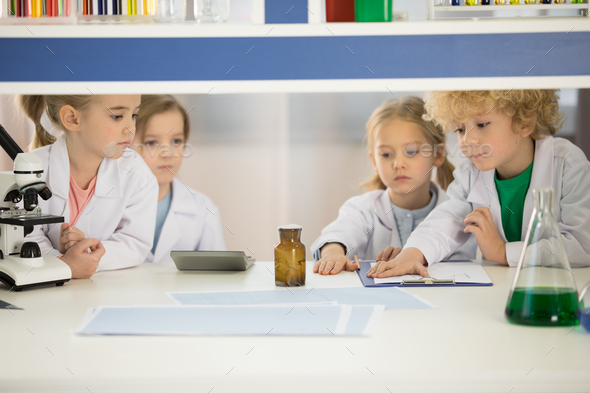 Schoolchildren in lab coats studying together in chemical laboratory ...