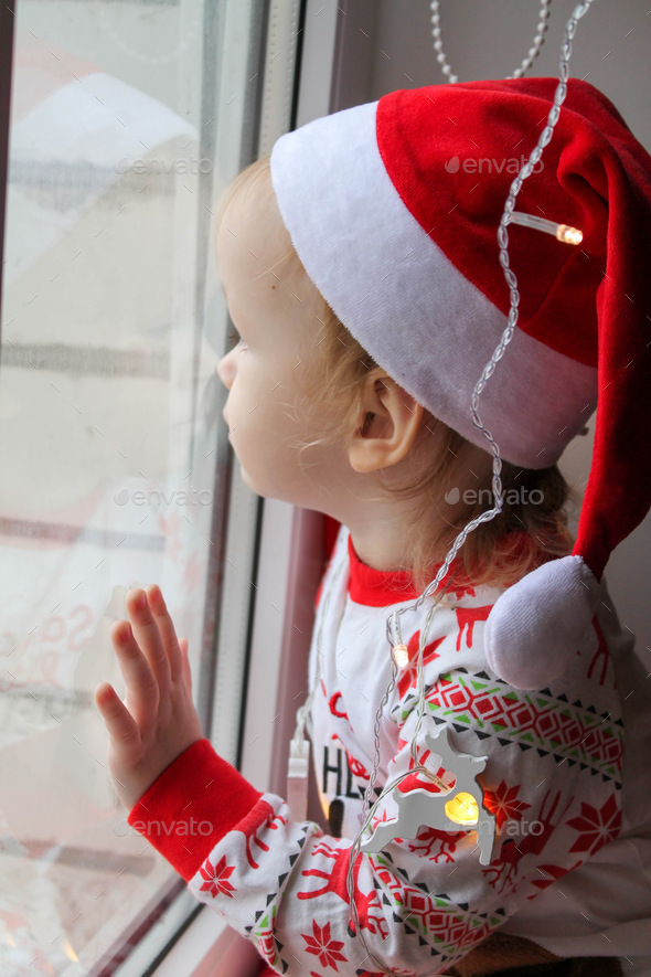 Cute baby girl in pyjama and red Santa Claus hat is sitting on the ...