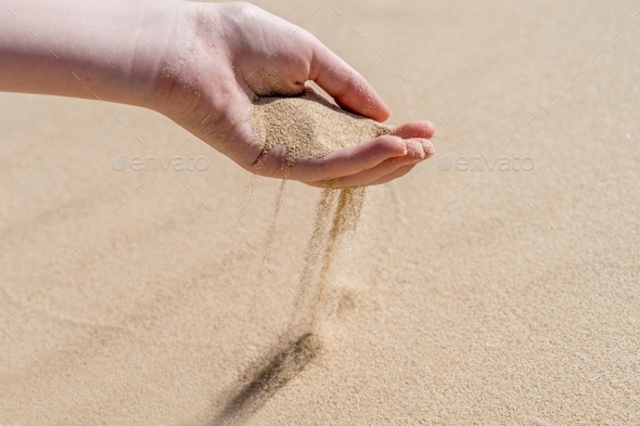 A hand pouring sand on a desert sand dune. Sand slips sifting through ...