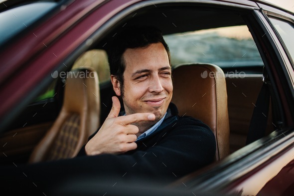 Man driving a car and pointing his finger out side in squinting his ...