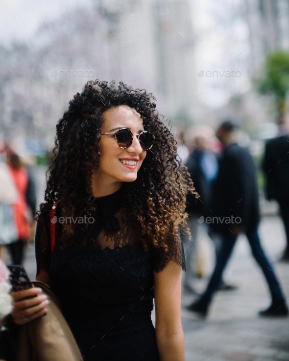 Beautiful young millennial woman with curly hair and sunglasses smiling ...