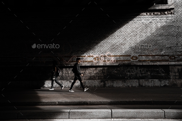 Two people walking under a bridge in shadow Stock Photo by Lemnaouer