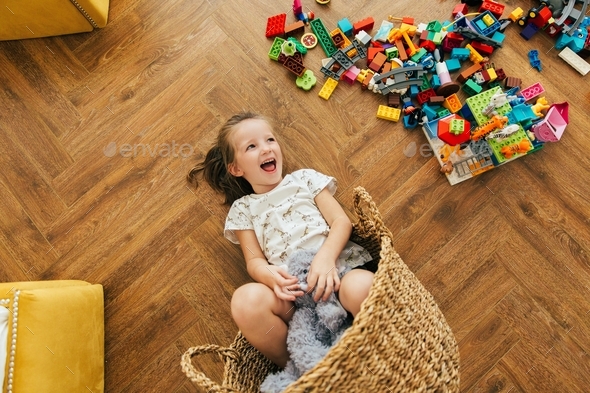 Happy girl poured Lego on the floor and lies in a basket and laughs ...