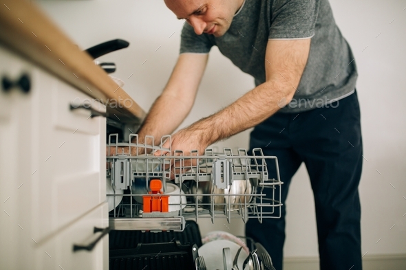 A man pulls out clean dishes from the dishwasher, a man does housework ...