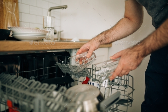 A man pulls out clean dishes from the dishwasher, a man does housework ...