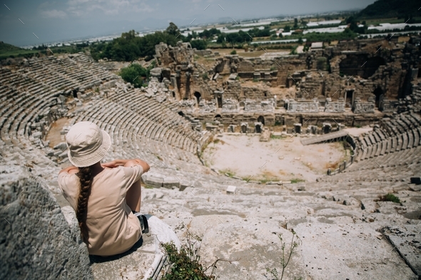 A teenage girl in a hat sits on top of an amphitheater in Perge, Turkey ...