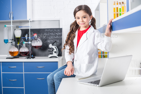 Beautiful little girl in lab coat using laptop in chemical laboratory ...
