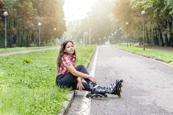 a girl on roller skates is resting sitting on the grass in the park ...