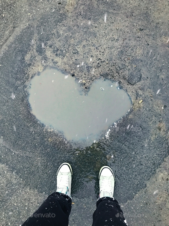 Standing at the heart shaped puddle under the falling snow Stock Photo by Leonteena