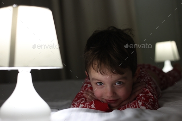 Nighttime sleep time. A boy in pajamas is lying in bed by the lamp ...