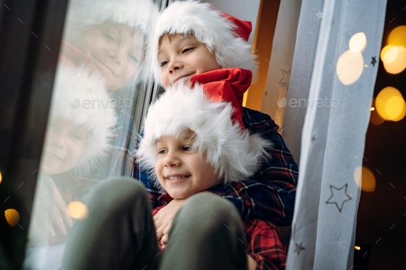 cute caucasian boys in red hats sitting on window sill and looking ...