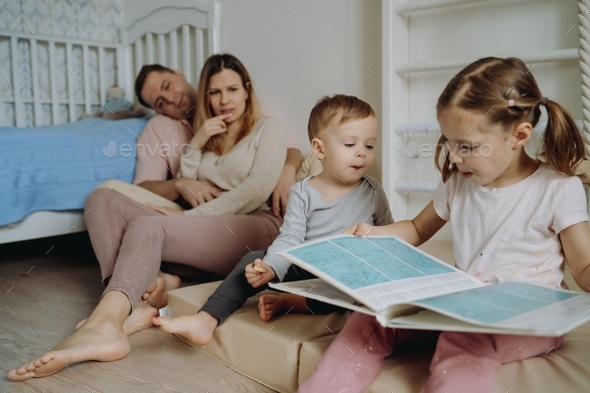 Parents watching with love their children reading a book together ...