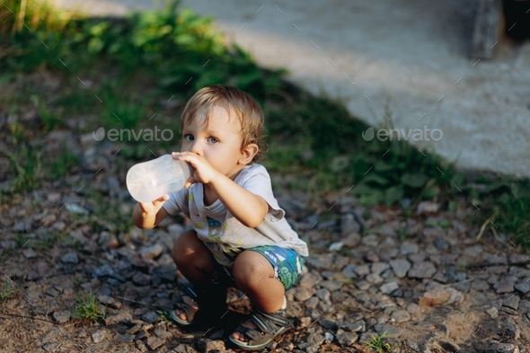 Cute little Caucasian boy sitting on haunches sipping water from baby ...