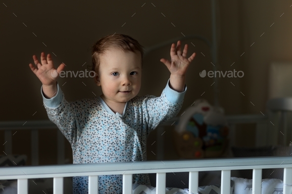 Cute baby boy standing in cote lifting hands up Stock Photo by uraneva