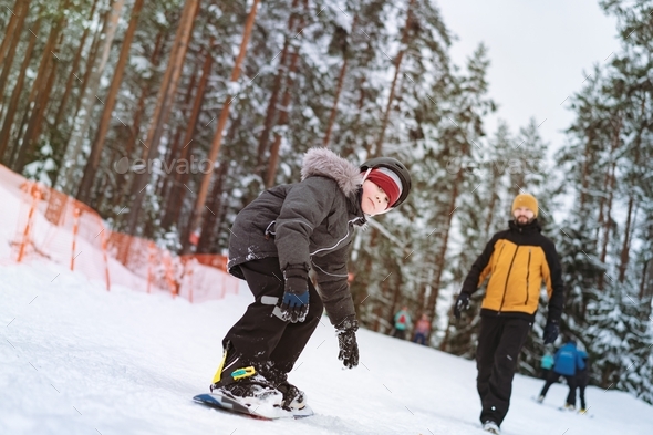 little boy learning to ride on snowboard on ski slope. Intructor ...