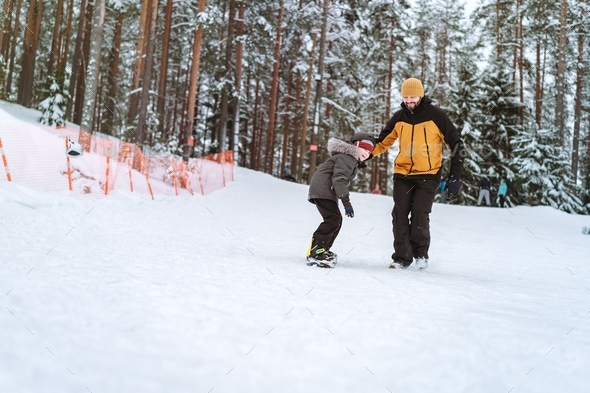 little boy learning to ride on snowboard on ski slope. Intructor ...