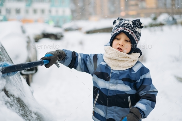 cute caucasian boy wearing scandinavian knit hat brushing snow from a ...