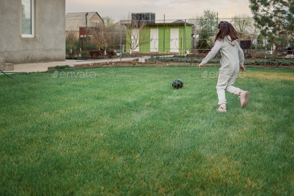 Cute little girl playing football with soccer ball on green lawn in ...