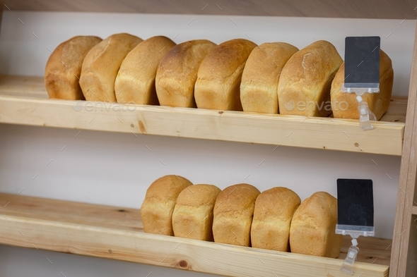 Bricks of wheat bread lie on wooden shelves in store. Fresh delicious ...