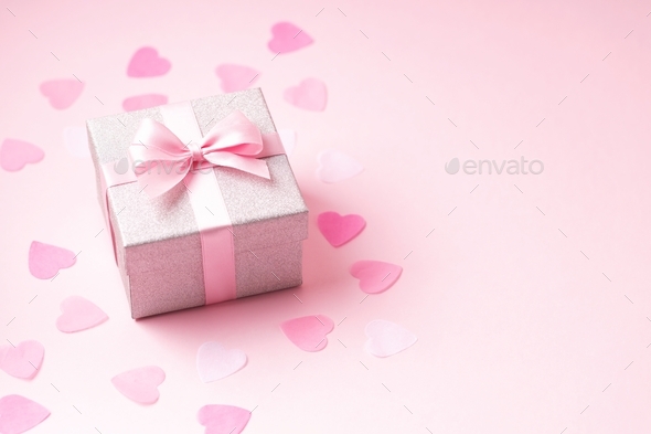 Silver glitter gift box with pink ribbon bow on pink background with ...